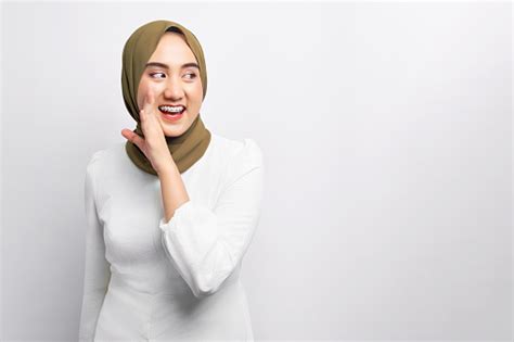 아름다운 행복한 젊은 아라비아 아시아 무슬림 여성이 히잡을 손에 입에 대고 비밀을 말하고 흰색 배경에 고립된 가십을 속삭이고