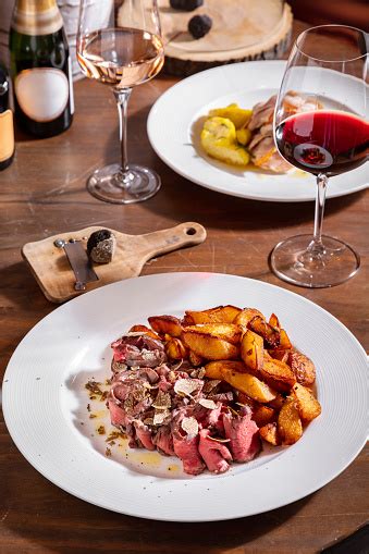 강판 트러플과 튀긴 감자를 곁들인 얇게 썬 고기와 와인 한 잔과 메인 코스가 테이블 위에 놓여 있습니다 0명에 대한 스톡 사진