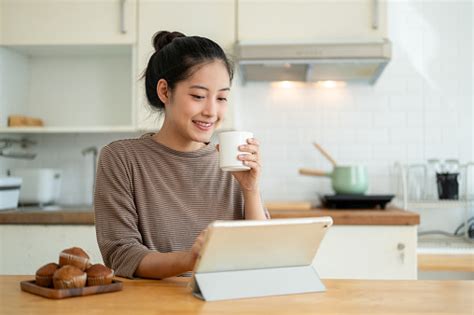 한 여성이 재택근무를 하며 커피를 마시고 부엌 테이블에서 태블릿을 사용하고 있다 20 24세에 대한 스톡 사진 및 기타 이미지 20 24세 가정 생활 가정 주방