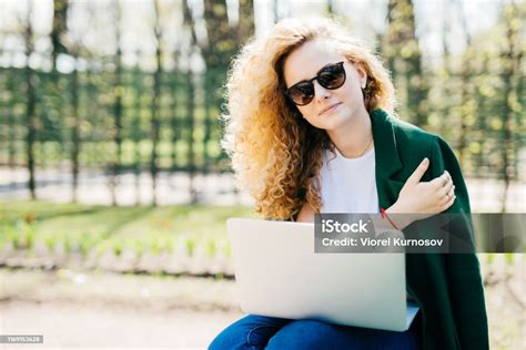 녹색 자연 배경을 통해 고립 된 그녀의 미래 프로젝트에서 일하는 무릎에 노트북을 들고 선글라스 흰색 티셔츠와 녹색 재킷을 입고