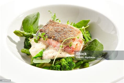 브로콜리와 녹색 시금치와 팬프라이드 피쉬 아스파라거스 에스푸마와 함께 건강한 구운 대구 흰색 배경에 고립 된 흰색 레스토랑 접시에 생선 튀김 건강한 생활방식에 대한 스톡