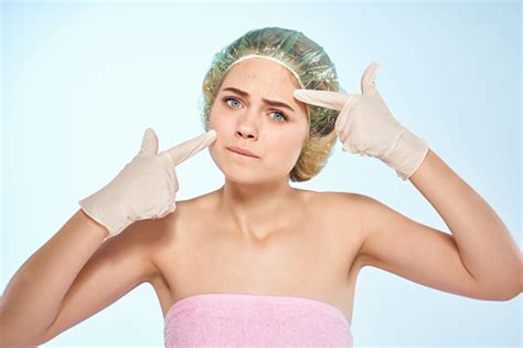 벌거 벗은 어깨 샤워 모자를 가진 여자는 그녀의 얼굴에 여드름을 짜냅니다 파란색 배경 16 17 살에 대한 스톡 사진 및 기타