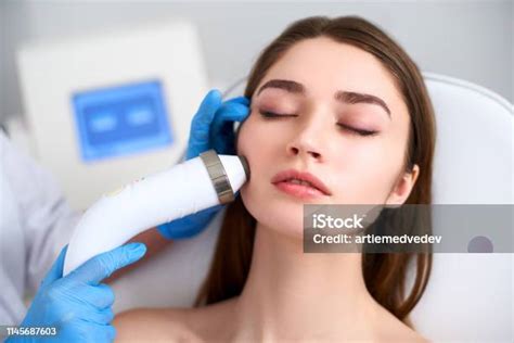뷰티 살롱에 누워 완벽 한 여자 얼굴에 대 한 Rf 리프팅 절차를 수행 미용사 의사 하드웨어 미용 환자는 전기 얼굴 마사지를 받습니다 피부 회 춘과 주름 완화 사람 얼굴에