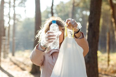 여성 운동가이자 조수가 쓰레기로 가득 찬 가방을 카메라에 보여주며 플라스틱 쓰레기로부터 숲을 청소하는 데 도움을줍니다 재활용 쓰레기 청소부에 대한 스톡 사진 및 기타 이미지