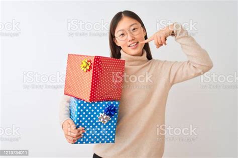 고립 된 흰색 배경 위에 생일 선물을 들고있는 젊은 중국 여성은 손가락 이빨과 입으로 쾌활한 모습과 가리키는 미소를 짓고 있습니다 치과 건강 개념 가리키기에 대한 스톡 사진