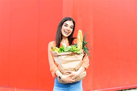 식료품으로 가득 찬 종이 가방을 들고 미소 짓는 아름다운 젊은 여성 빨간 배경 위에 식료품 가방을 들고 행복한 예쁜 소녀 나름에 대한 스톡 사진 및 기타 이미지 Istock