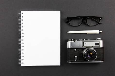 현대 사무실 직장 플랫은 어두운 검은 색 배경에 빈 나선형 종이 노트북 모형 복고풍 카메라 펜 및 독서 안경으로 놓여 있습니다 상단 보기 공간을 복사합니다 0명에 대한 스톡