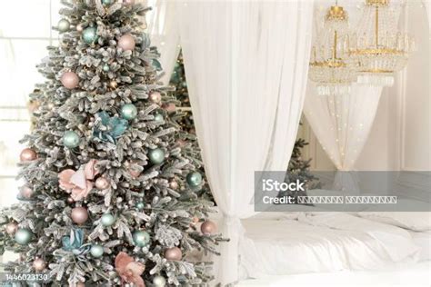 흐르는 흰색 커튼이 있는 침대와 다이아몬드의 많은 유리 크리스탈이 빛나는 크리스탈 샹들리에가 있는 현대적인 흰색 침실 축제 장식 크리스마스 트리입니다 인테리어 디자인 침실