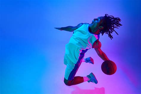 네온 불빛의 그라데이션 파란색 배경에 공을 들고 점프하는 프로 농구 선수의 역동적인 이미지 18 19세에 대한 스톡 사진 및