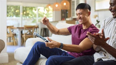 Same Sex Male Couple Or Friends On Sofa At Home With Handheld Mobile