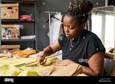 Young Serious Seamstress With Scissors Cutting Textile Of Yellow Color