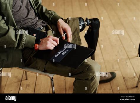 Young Man With Disability Holding Black Folder Of Ptsd Support Group While Sitting On Chair
