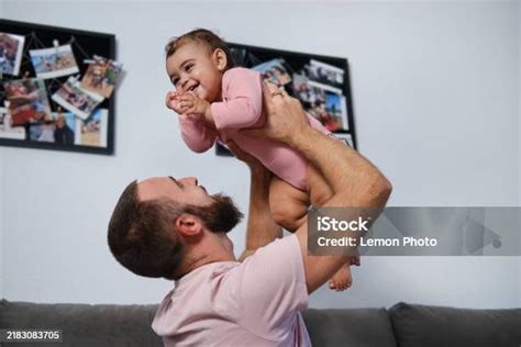 자랑스러운 백인 유럽 남자가 집 거실에서 어린 딸을 공중으로 들어 올리는 측면 사진 개념 가족과 부성 2명에 대한 스톡 사진 및