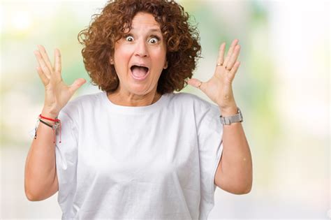 아름 다운 중간 어른 고위 여자에 흰색 티셔츠를 입고 미친 축 하 배경 절연 및 팔 제기 성공을 위한 놀라게 했 고 눈 흥분