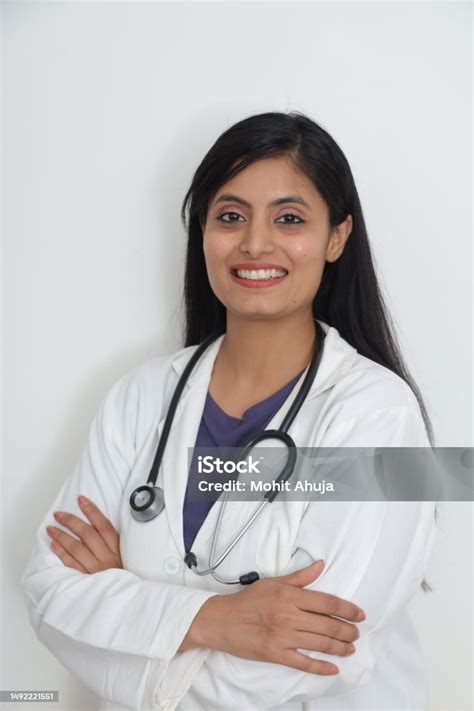 실험복을 입은 인도의 고위 여성 의사의 초상화는 파란색 배경에 팔짱을 끼고 있다 흰 코트를 입은 행복한 인도 의사가 병원 배경에 웃고 있다 여자 의사에 대한 스톡 사진 및