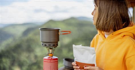 젊은 여성은 여름에 산을 여행하는 동안 가스 버너가 있는 밀폐 패키지로 하이킹을 위해 동결 건조 음식을 준비합니다 하이킹 중 음식 개념 사진 Unsplash의 여성