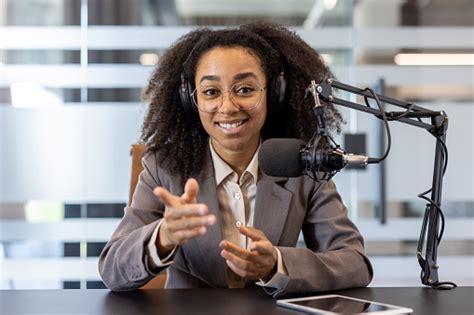 양복을 입은 젊은 아프리카계 미국인 여성이 헤드폰을 끼고 마이크가 있는 스탠드 뒤에 앉아 카메라를 향해 말하고 몸짓하는 모습 가상현실에 대한 스톡 사진 및 기타 이미지