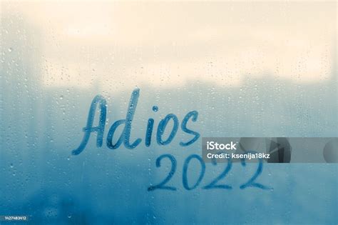 스페인어로 Adios를 쓰는 것은 영어로 작별 인사를하고 숫자 2022는 일몰 창문에 비 안개가 자욱한 유리로 튀어 나온 물