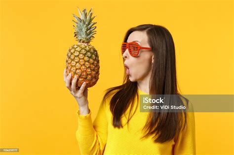 스튜디오에서 노란색 오렌지 배경에 고립 된 손으로 신선한 잘 익은 파인애플 과일을 보고 재미 안경 젊은 여자 충격 사람들은 생생한 라이프 스타일 휴식 휴가 개념입니다 복사