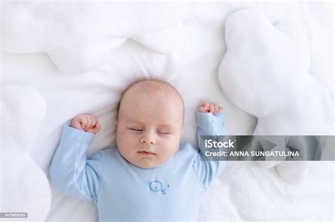 Мальчик Спит На Кровати Лежа На Спине В Синей Пижаме С Поднятыми Руками Среди Подушек Облаков