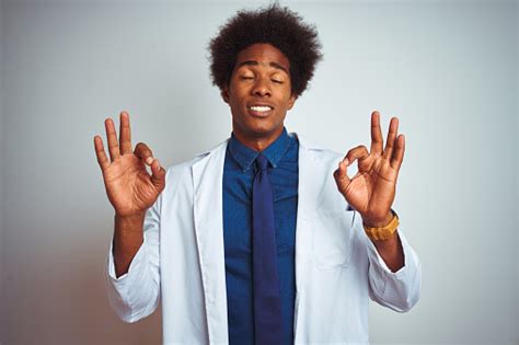 고립 된 흰색 배경 위에 서있는 코트를 입은 젊은 아프리카 계 미국인 의사가 손가락으로 명상 제스처를하고 눈을 감고 미소 요가 개념입니다 개념에 대한 스톡 사진 및 기타