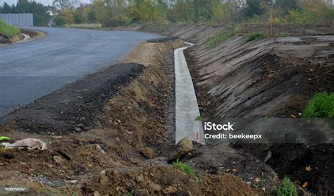 새로 지어진 도로로 그 층에는 스크 리드와 아스팔트 카펫이 연속적으로 보입니다 주변 지역은 콘크리트 홈통이있는 도랑으로 경사져 있습니다 빗물 배수 도랑 인도에 대한 스톡