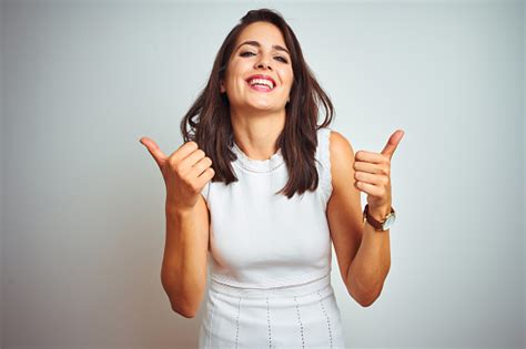 흰색 고립 된 배경 성공 표지판 위에 서있는 드레스를 입은 젊은 아름다운 여성은 손으로 긍정적 인 제스처를하고 엄지 손가락으로 미소와 행복을 합니다 쾌활한 표정과 승자