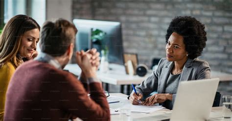 아프리카계 미국인 은행 관리자는 사무실에서 대출과 관련된 상담 중에 부부와 의사 소통합니다 사진 Unsplash의 세르비아 이미지