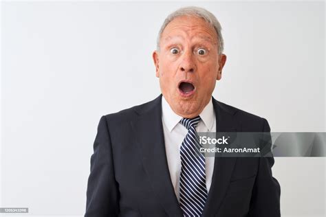 고립 된 흰색 배경 위에 서있는 양복을 입은 선임 회색 머리 의 사업가는 놀라움의 표정 두려움과 흥분된 얼굴로 충격을 받았습니다 쇼크에 대한 스톡 사진 및 기타 이미지