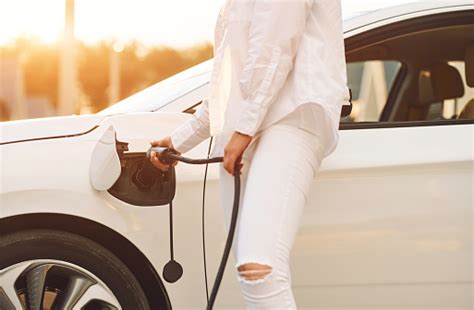 충전기 유지 흰 옷을 입은 젊은 여자는 낮에 전기 자동차와 함께 있다 35 39세에 대한 스톡 사진 및 기타 이미지 35 39세 고급 깨끗한 Istock