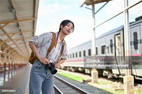 แบ็คแพ็คเกอร์หญิงพร้อมกระเป๋าเป้สะพายหลังและกล้องของเธอยืนอยู่ที่ชานชาลาเพื่อรอรถไฟขอ ภาพสต็อก