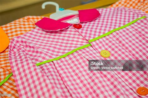 밝은 녹색 테두리 여러 가지 빛깔의 단추 핫핑크색 칼라가 있는 분홍색 깅엄 아동용 작업복을 클로즈업하여 직물이나 교복을 전시하기 위해 카운터에 놓았습니다 Diy에 대한 스톡