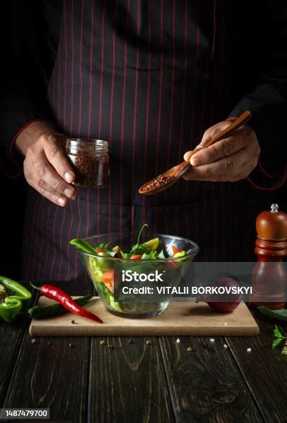 요리사는 신선한 야채로 채식 요리를 준비합니다 어두운 배경에 있는 호텔의 메뉴 개념입니다 샐러드에 건조한 향기로운 향신료를 추가합니다 가정 주방에 대한 스톡 사진 및 기타