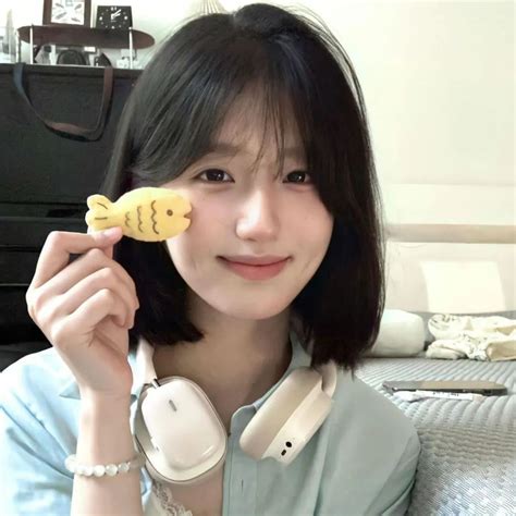 女孩手持可爱小鱼玩偶，头戴耳机笑容甜美 男女头像｜简单又好看的微信头像表情包图片动图 求表情网 斗图从此不求人