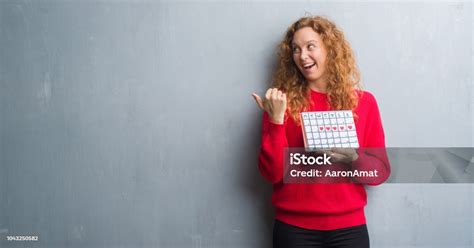 고 행복 얼굴 미소와 측면까지 손가락으로 보여주는 기간 일정을 잡고 회색 그런 지 벽에 빨강 머리 젊은 여자 가리키기에 대한 스톡 사진 및 기타 이미지 Istock