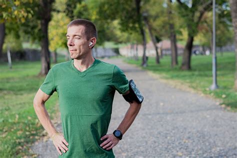 정신 건강 및 자기 관리 활동의 일환으로 공공 공원에서 야외에서 부드러운 일상 운동을하는 행복한 운동 중반 성인 남성 그는 운동복과 스마트 워치를 착용하고 있습니다 그는