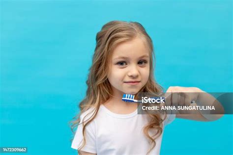 흰색 티셔츠를 입은 귀여운 어린 소녀는 파란색 배경에 칫솔로 이빨을 닦고 위생과 치과의 개념 텍스트 공간 아이에 대한 스톡 사진