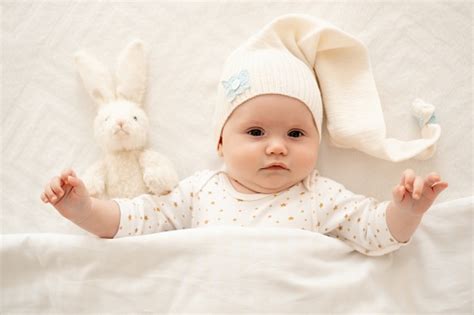 담요 아래 수면 모자를 쓰고 잠자리에 들기 전에 행복한 신생아가 침대에 누워 침실의 하얀 침대에서 미소를 짓고 있는 행복한 귀여운 작은 아기 평면도 2 5 개월에 대한 스톡