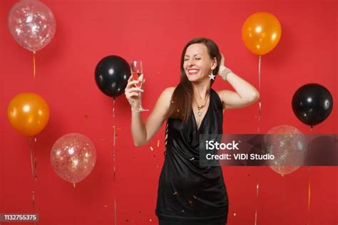 밝은 빨간색 배경 공기 풍선에 머리에 손을 넣고 샴페인 잔을 들고 축 하 하는 검은 드레스에 매력적인 웃는 여자 새 해 복 많이 받으세요 생일 이랑 휴일 파티 컨셉 2019