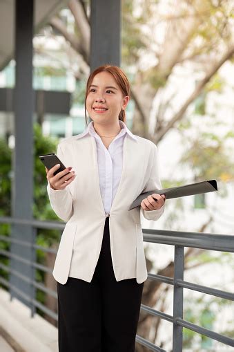 쾌활한 사업가가 스마트폰과 파일을 들고 모던한 오피스 공간에 서 있다 Brand Name Smart Phone에 대한 스톡 사진 및 기타 이미지 Brand Name