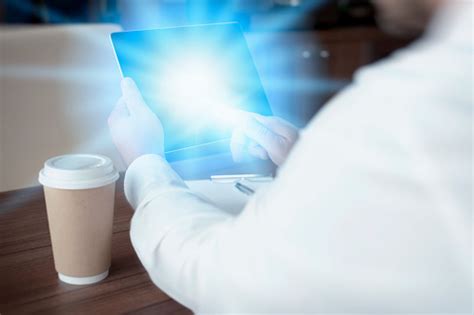 화면에 광선이 달린 흰색 셔츠를 입은 사업가가 디지털 태블릿을 손에 들고 있는 프리랜서 사업가 기술 개념 커피 한 잔과 함께 작업장 개념에 대한 스톡 사진 및 기타 이미지