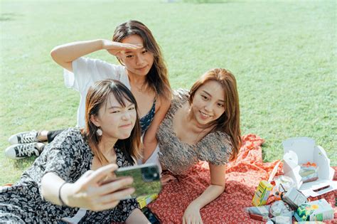 공원의 풀밭에 앉아 스마트 폰으로 셀카를 찍는 세 명의 젊은 아시아 여성 친구 3 명에 대한 스톡 사진 및 기타 이미지 3 명 소풍 음식 스마트폰 Istock