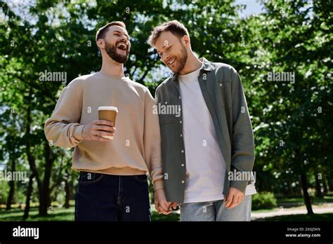A Bearded Gay Couple Walks Through A Green Park Laughing And Enjoying