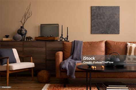 갈색 소파 둥근 커피 테이블 책 슬리퍼 검은 사다리 공 무늬가 있는 카펫 베개 및 개인 액세서리가 있는 아늑한 거실의 인테리어