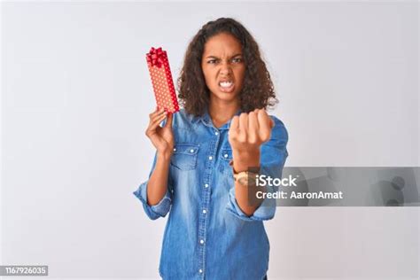 고립 된 흰색 배경 위에 서있는 발렌타인 선물을 들고있는 젊은 브라질 여성은 화가 나고 화가 나서 분노로 외치고 미친 듯이 고함치고 분노 개념으로 감정에 대한 스톡 사진 및