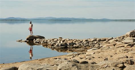 알아볼 수 없는 셔츠를 입지 않은 젊은 남자가 바위 위에 서서 아름답고 맑은 여름날 평화로운 호수 전망을 즐기고 있다 사진 Unsplash의 바닷가 이미지