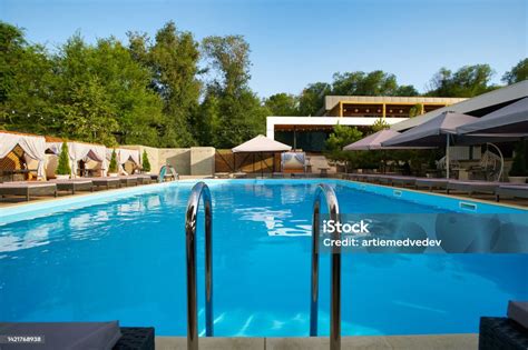 고급 리조트의 수영장 옆을 따라 사다리 전망대 갑판 의자 및 태양 우산이있는 수영장 지역 녹지로 둘러싸인 여름 주택 평온함과 휴가 중 편안한 분위기 가장자리에 대한 스톡