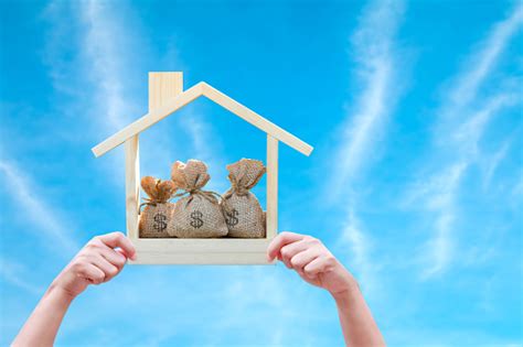 여성 핸드 홀딩은 푸른 하늘과 구름 배경 비즈니스 투자 및 부동산 개념에 대한 대출 자본 관리를 작동하는 돈 가방이있는 홈 모델의 레이블을 보여줍니다 가방에 대한 스톡 사진