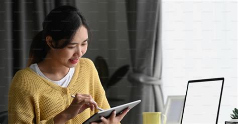 젊은 여성이 스타일러스 펜을 들고 태블릿 화면을 가리키며 사무실에서 흰색 화면이 있는 노트북 앞에 앉아 있다 사진 Unsplash의 태국 이미지