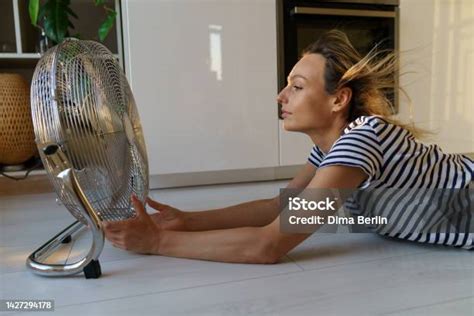 땀을 흘리는 여성이 장치를 향해 머리를 들고 바닥에 누워 팬을 잡고 차가운 기류를 잡으려고합니다 30 34세에 대한 스톡 사진 및 기타 이미지 Istock
